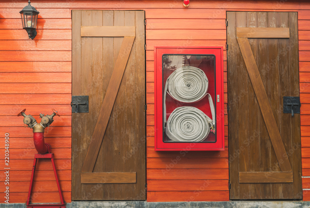 Fire hose in red cabinet hanging on orange wooden wall. Fire emergency ...