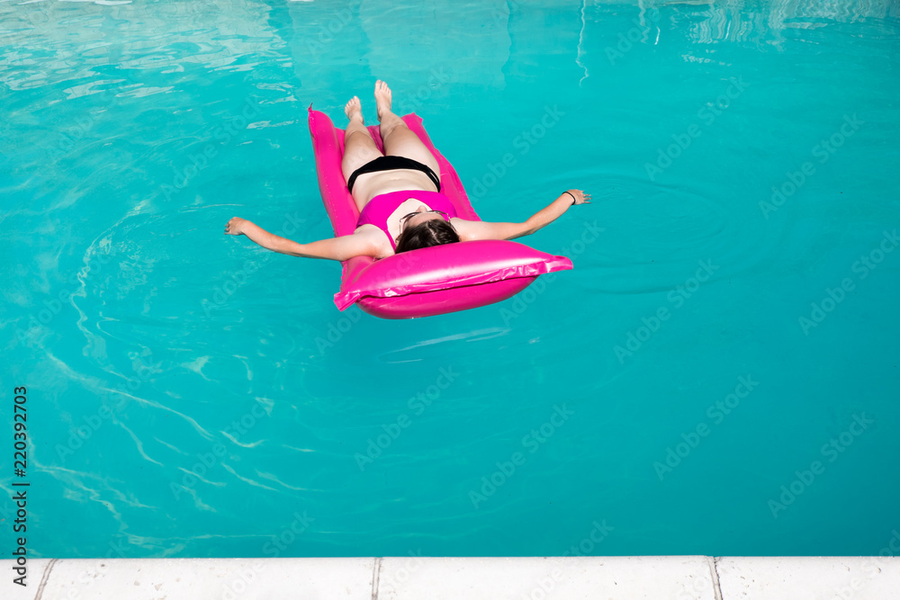 Beautiful woman floating on a bright pink raft in an outdoor swimming ...