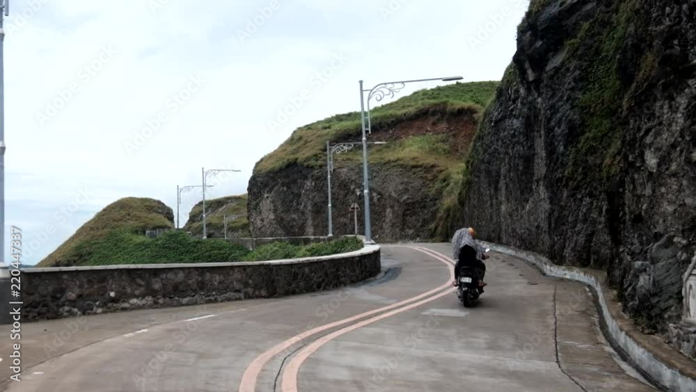 Motorcycle with two people driving past the camera in a curved road in ...