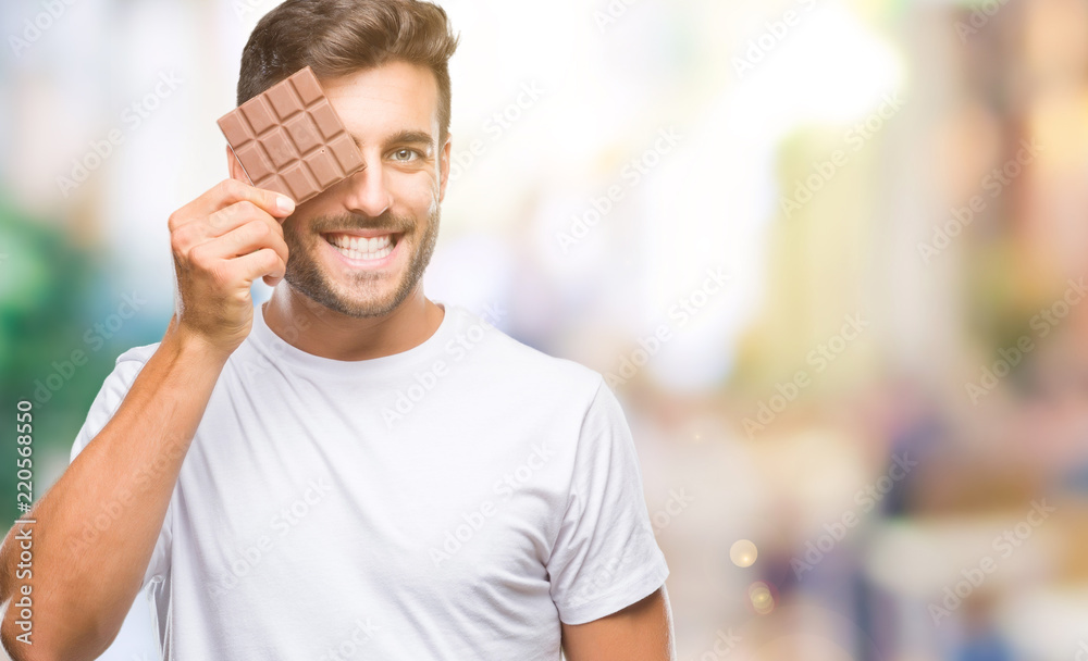 Young handsome man eating chocolate bar over isolated background with a ...