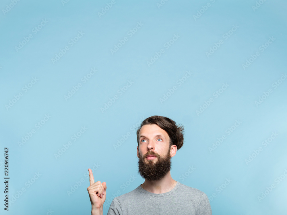 young man pointing up above his head to a virtual object or text. copy ...