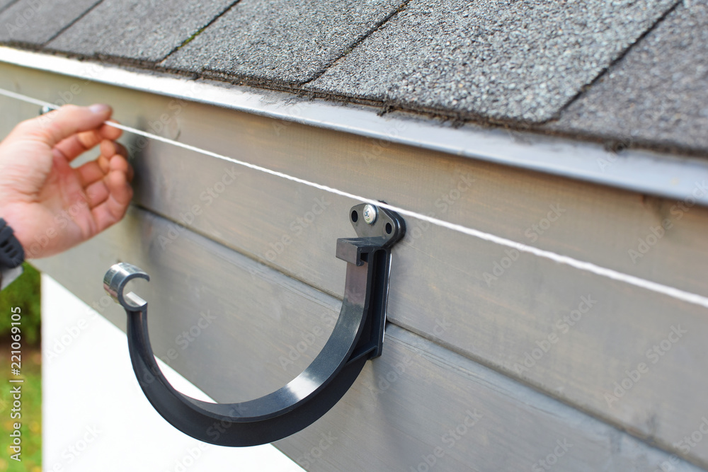 Man hands installing dark grey plastic roof gutter holder on wooden ...