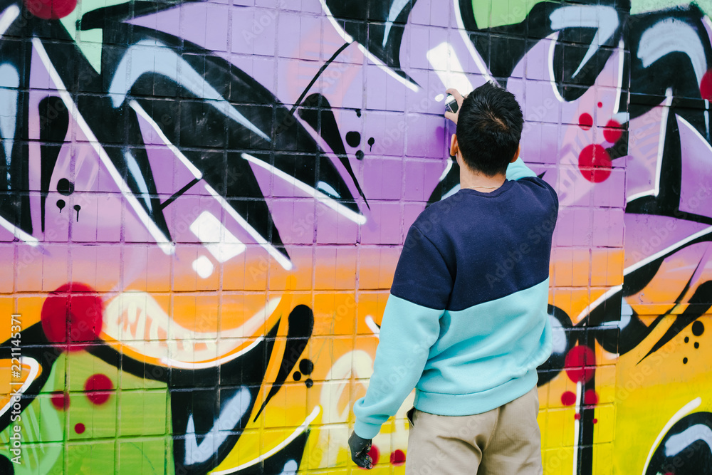 Young man graffiti artist painting on the wall | Uwalls.co.uk