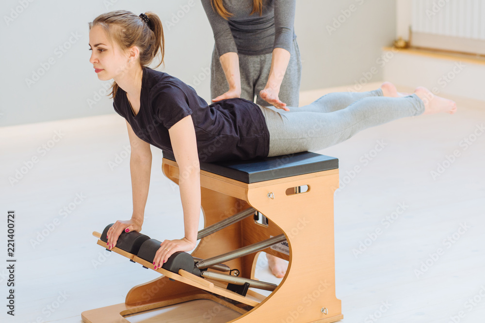 Female instructor of pilates helping to young woman workout on chair ...