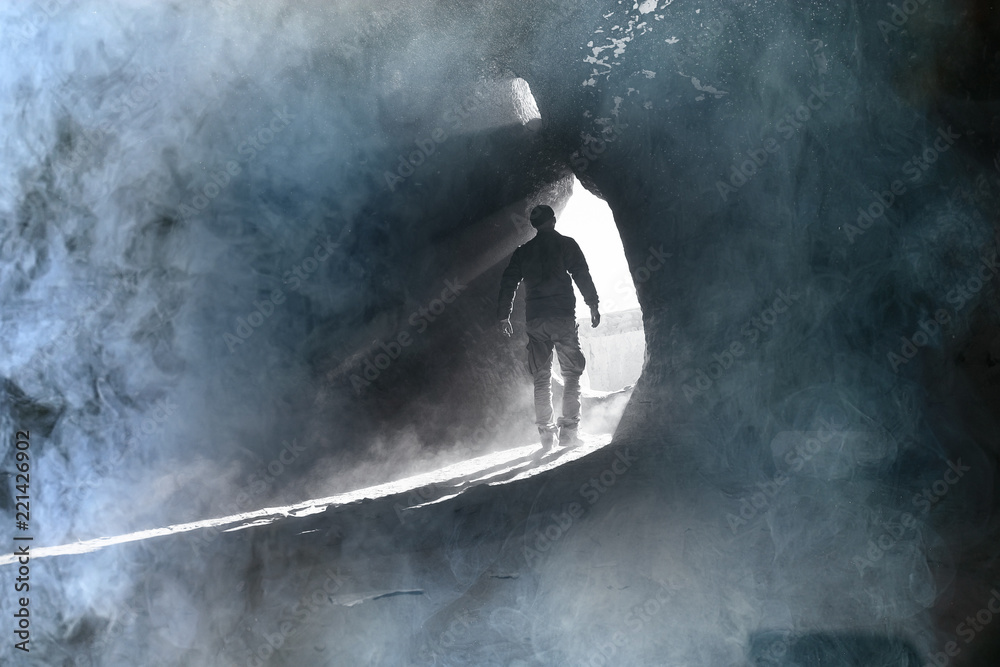 entrance to the cave, a male traveler stands in the rays of light at ...