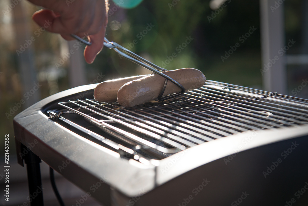 Mann grillt und dreht Bratwurst auf elektronischen Grill mit Grillzange ...