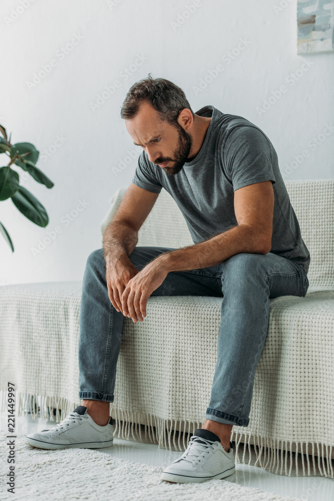 full length view of depressed bearded man sitting on couch and looking ...