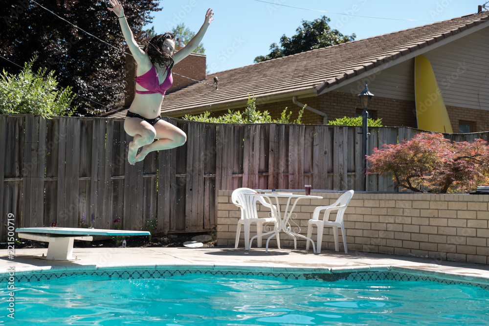 Young brunette woman jumps off diving board arms up in the air into an ...
