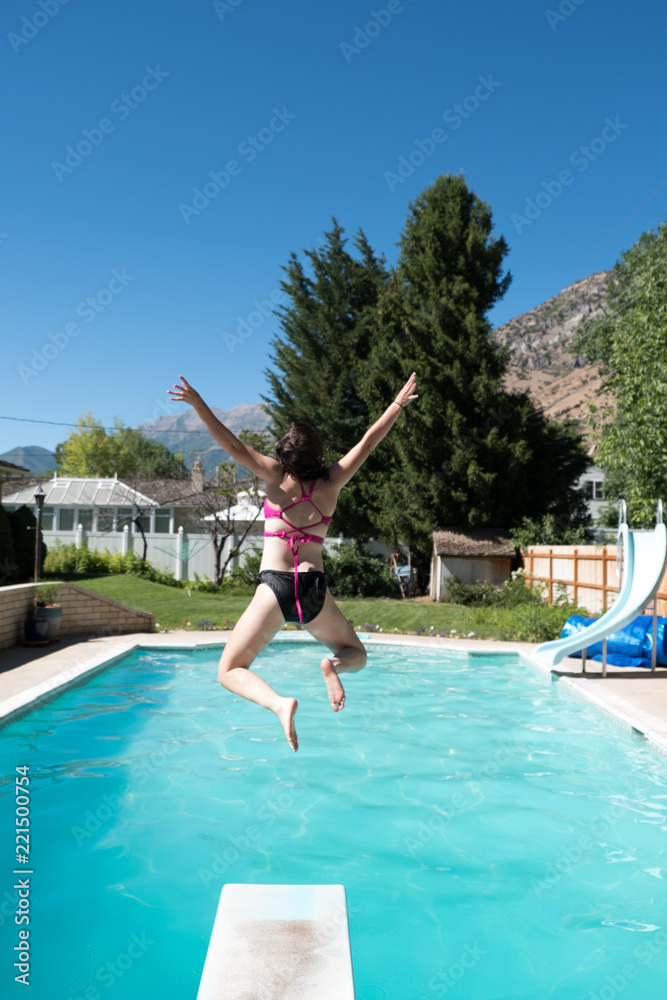 Young woman jumps off diving board into a backyard swimming pool. Woman ...
