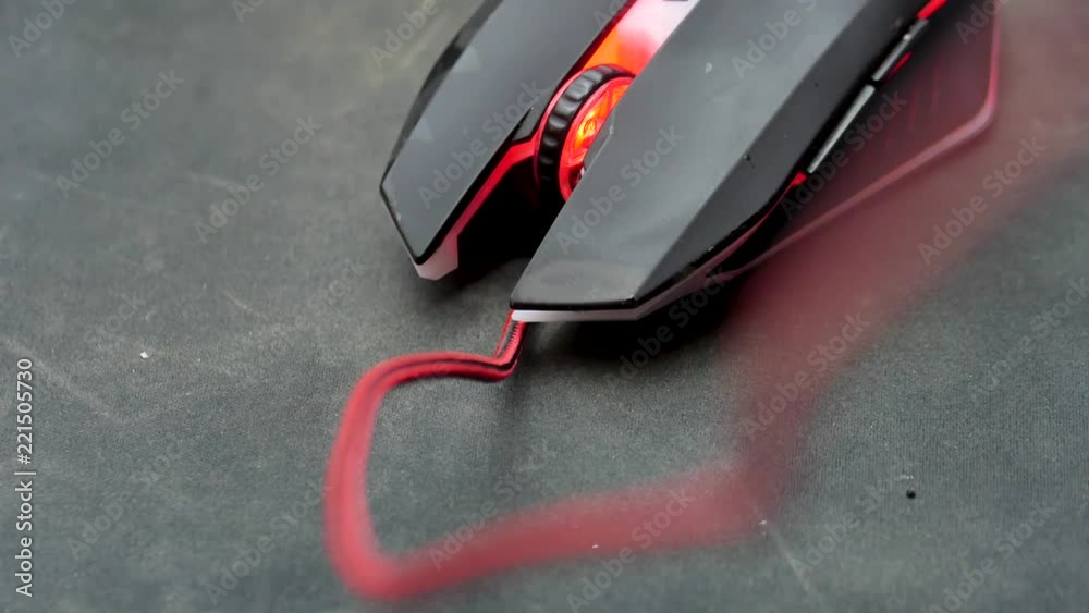 Red gaming mouse on a mouse pad. The cable goes forward in front of the ...