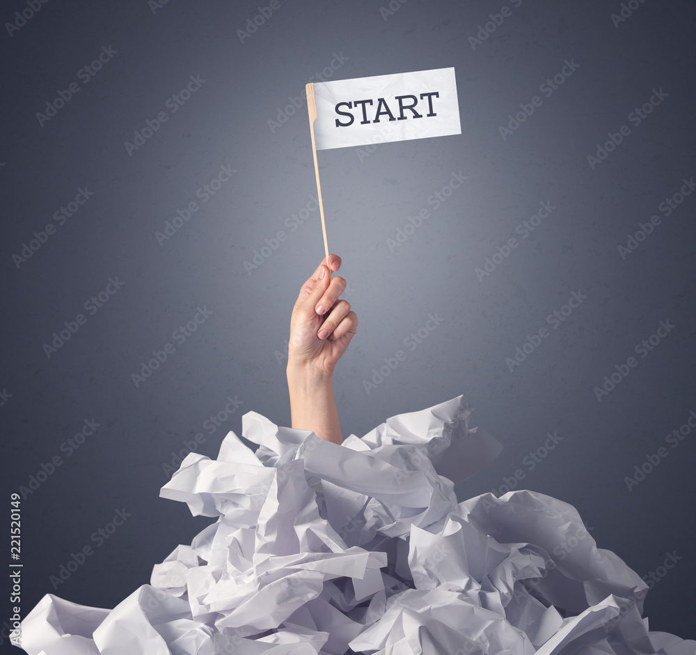 Female hand emerging from crumpled paper pile holding a white flag with ...