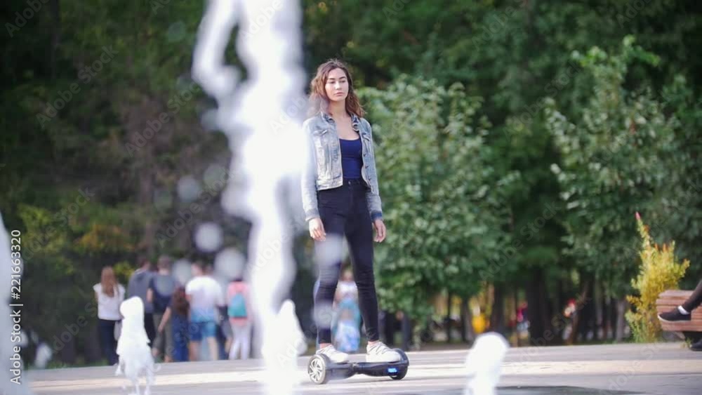 Beautiful slender girl with long hair rides a gyroscope in the park ...