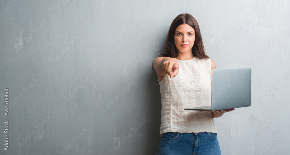 Young brunette woman over grunge grey wall using computer laptop ...