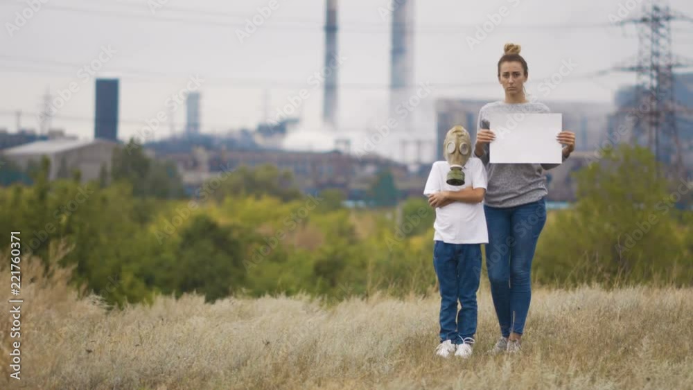 Mom and son in a gas mask stand in the background of a factory and ...