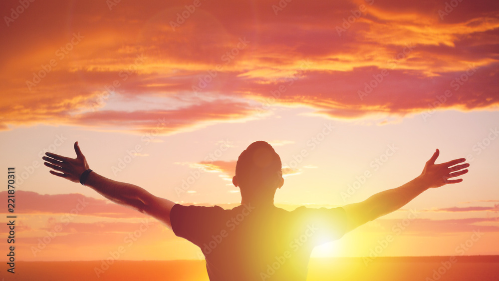 Young man standing outstretched at sunset. Bright solar glow and sky ...