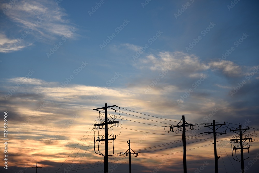 Sunset over a row of utility poles and high voltage overhead power ...