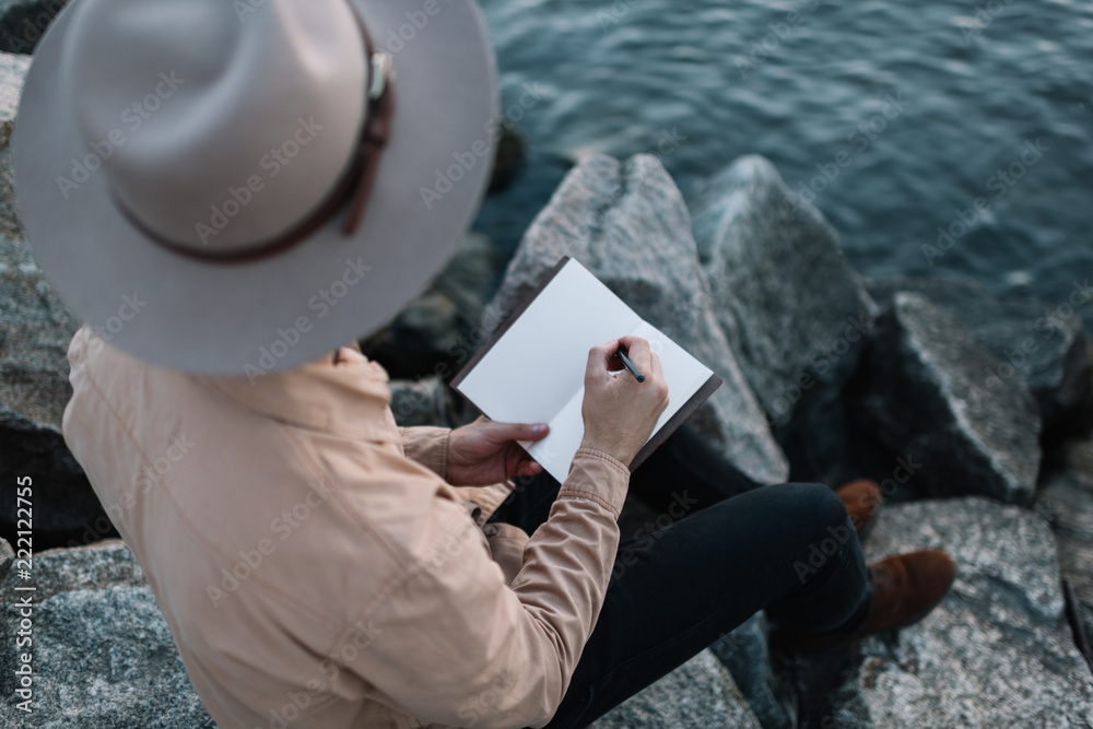 Traveller wearing stylish clothes and hipster hat writing notes in ...