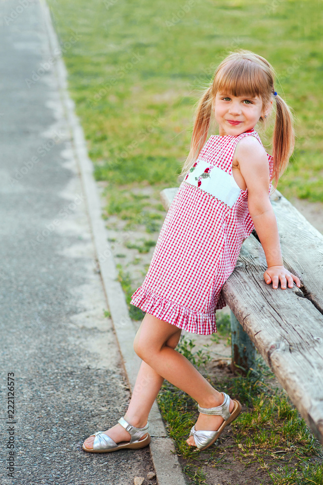 Little girl with two ponytails in red dress is walking outside. Happy ...
