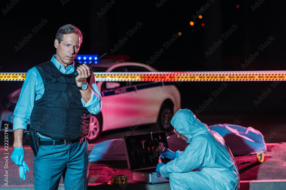 mature male police officer talking on radio set while criminologist ...