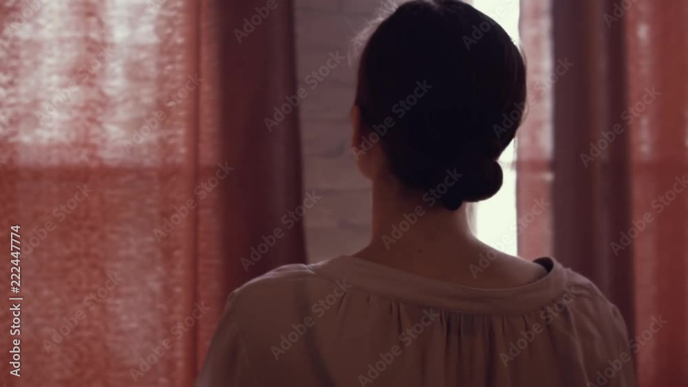 Girl approaches large panoramic window and shades it. Young girl with ...