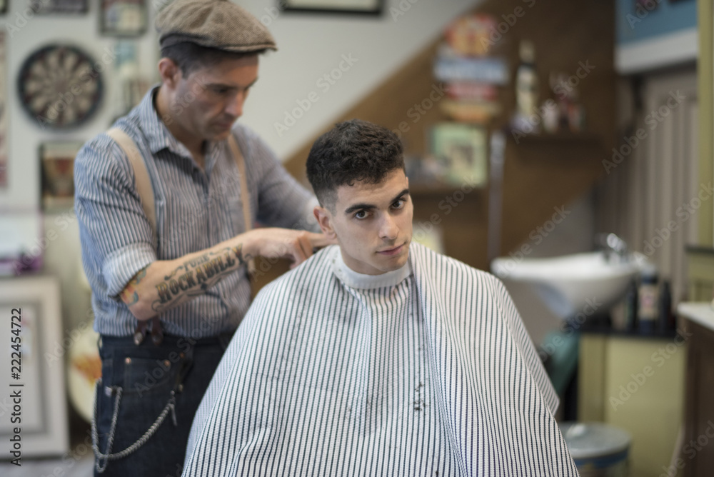 Foto de Barbero moderno con vestimenta vintage corta el pelo a joven ...