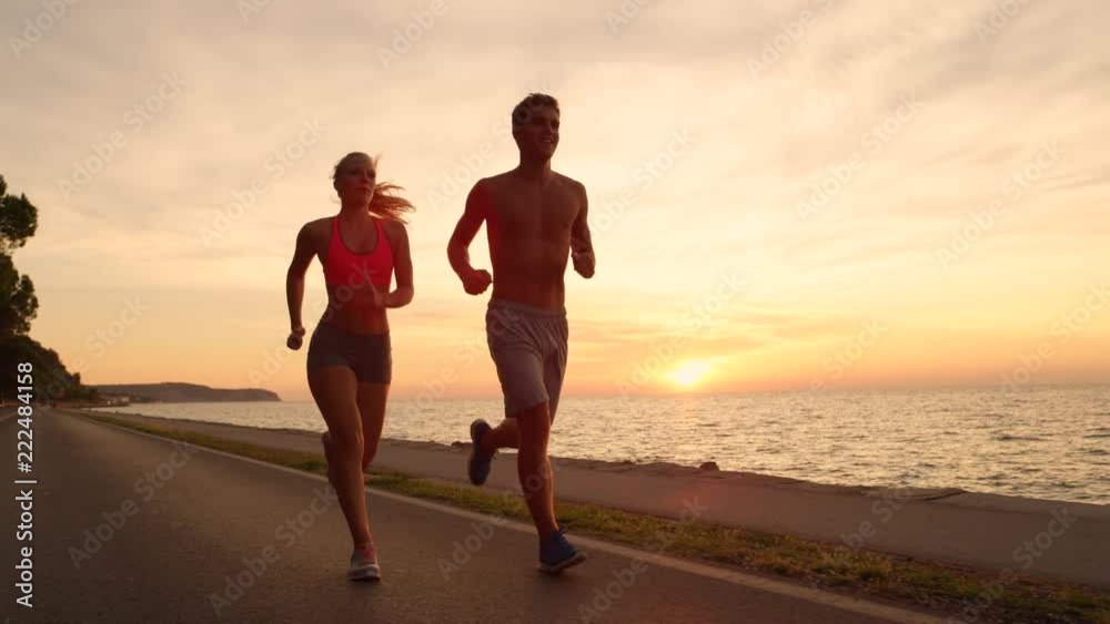 SLOW MOTION, LENS FLARE: Happy fit couple jogging down the coastal road ...