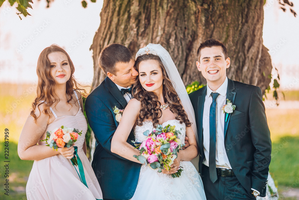 Newlyweds and their friends open champagne bottle standing in the park ...