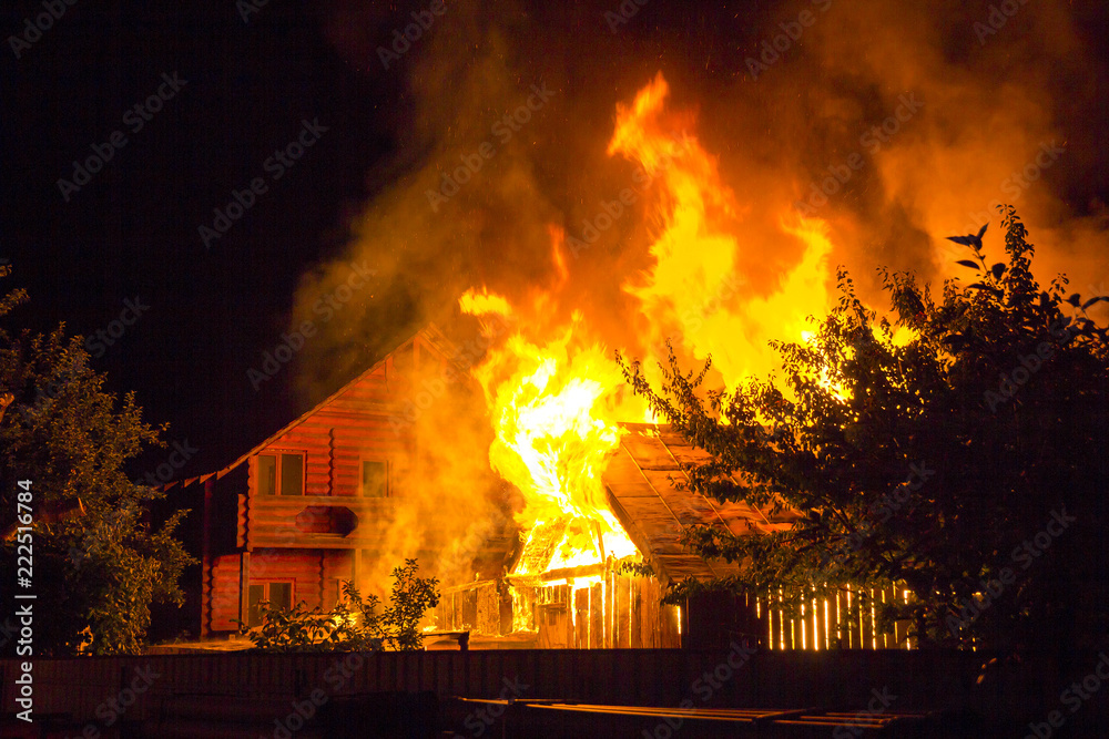 Burning wooden house at night. Bright orange flames and dense smoke ...