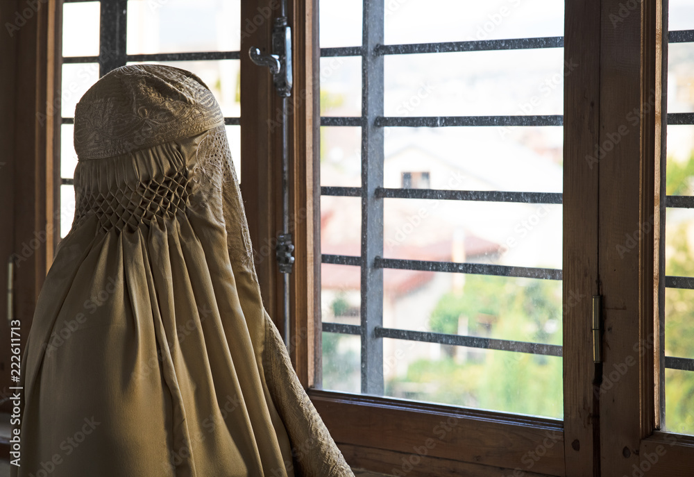 Indoors shot of a person wearing a gold-coloured Burqa looking through ...