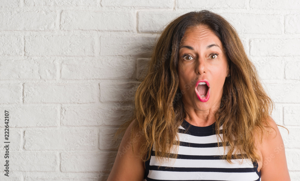 Middle age hispanic woman over white brick wall scared in shock with a ...