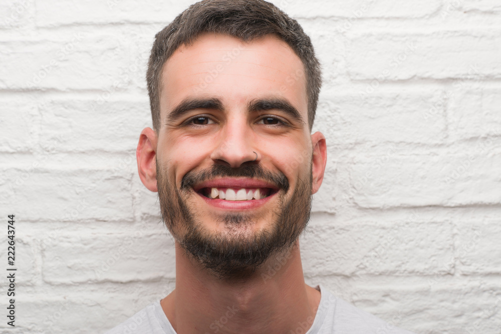 Young adult man standing over white brick wall with a happy face ...