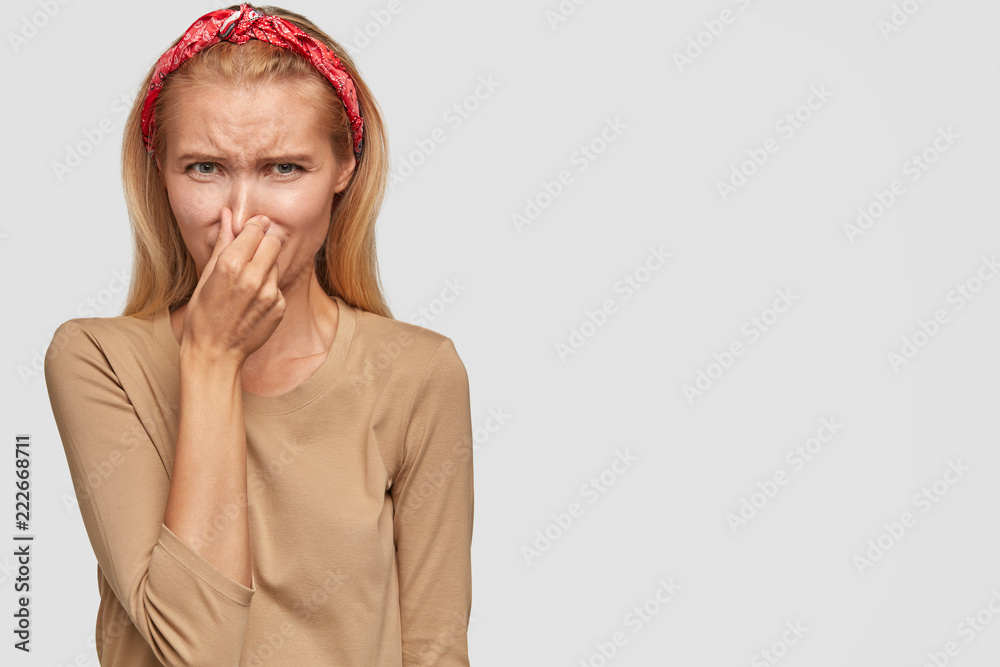 Discontent woman with displeased look covers nose as smells stench or ...