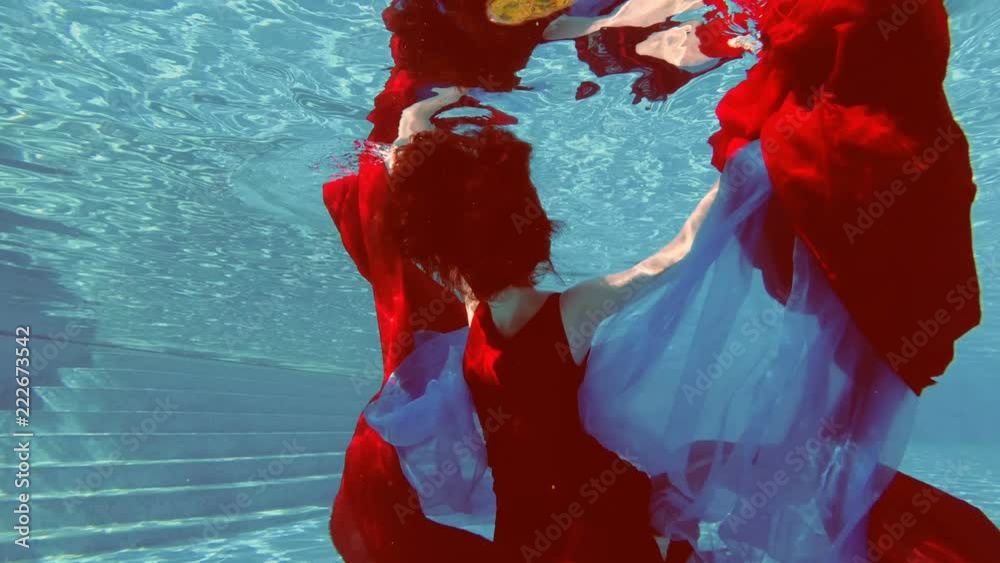 A beautiful girl in a red dress with red hair swims and poses ...