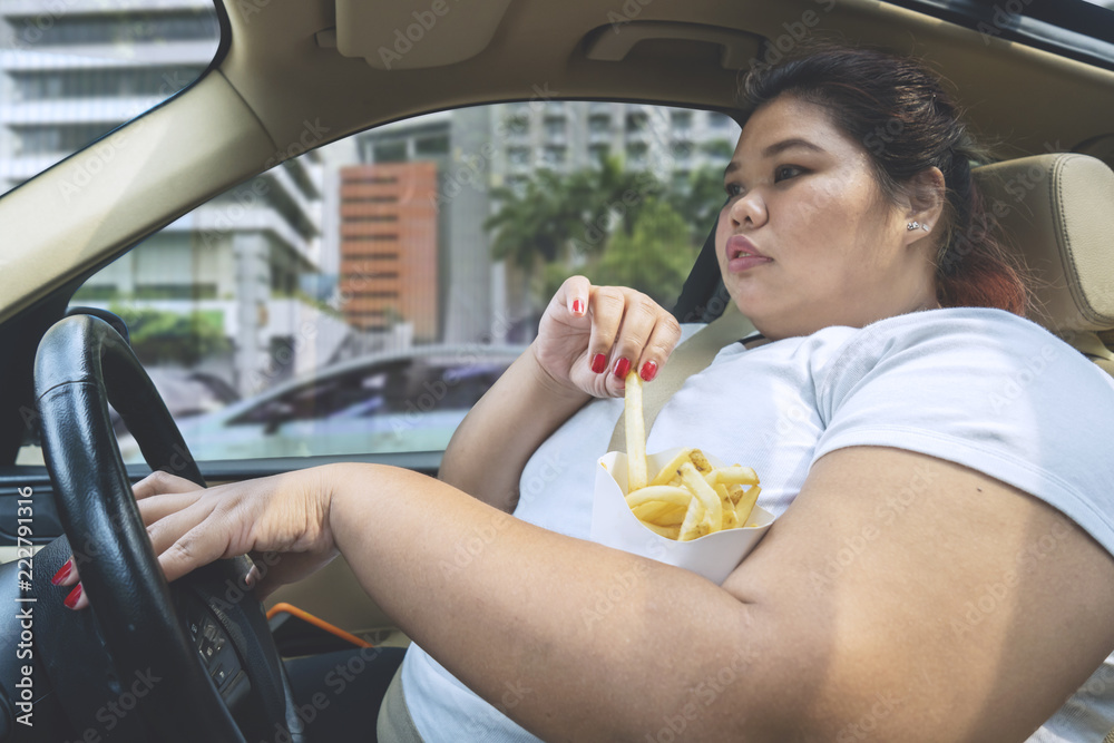 Overweight woman eats french fries inside a car Stock Photo | Adobe Stock