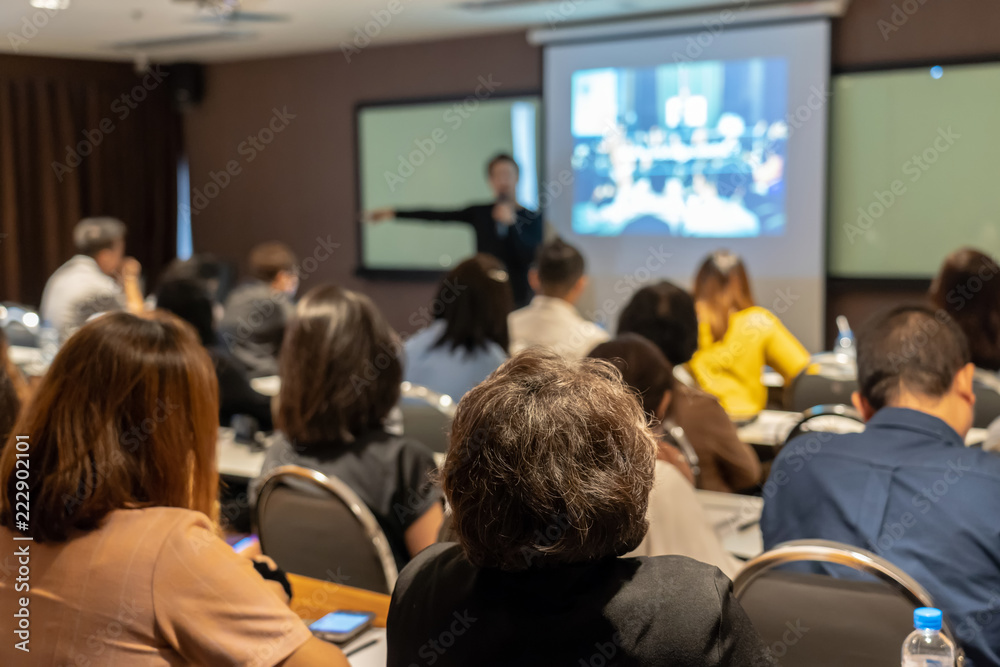 Back side of audience listening the Asian Speaker with casual suit on ...