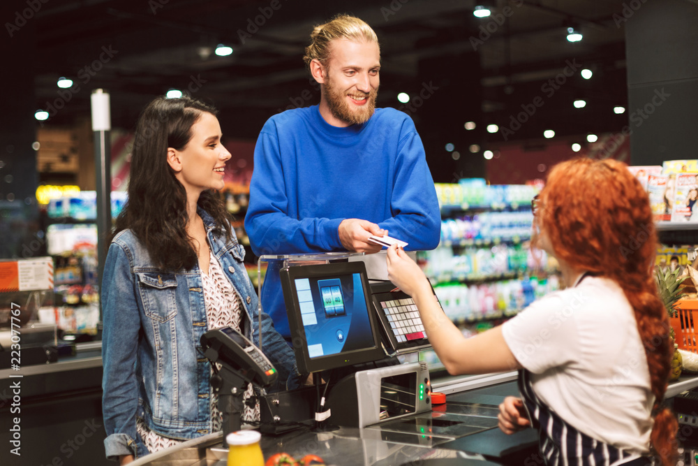 Young cheerful couple standing near cashier desk while happily giving ...