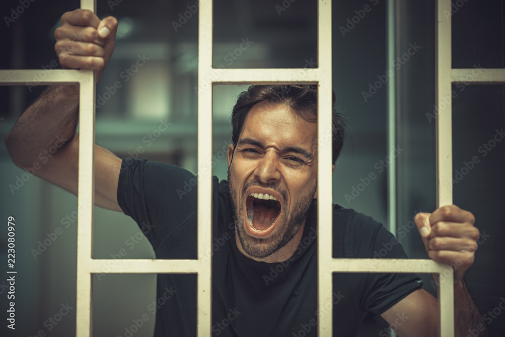 Solitude concept, man behind prison or cage bars trying to break free ...