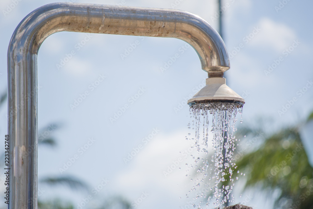 Medium close up standing under an outside swimming pool shower under a ...