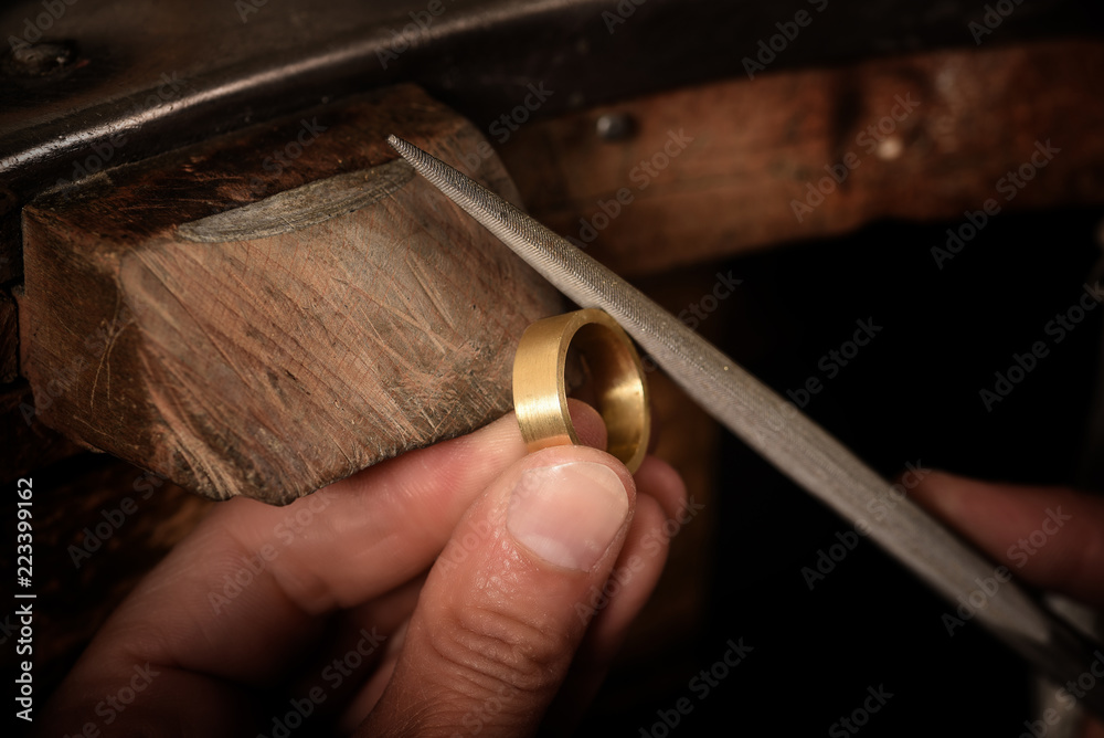 Foto de goldsmith hand holds a golden ring on the wooden workbench and ...