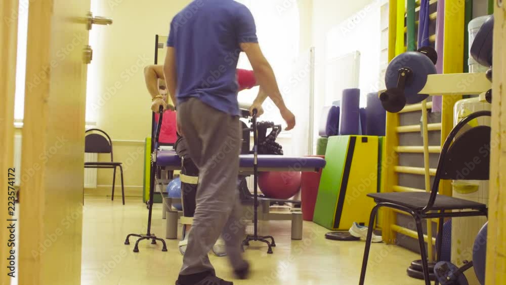 Young disable man in orthosis getting up with support of two walking ...