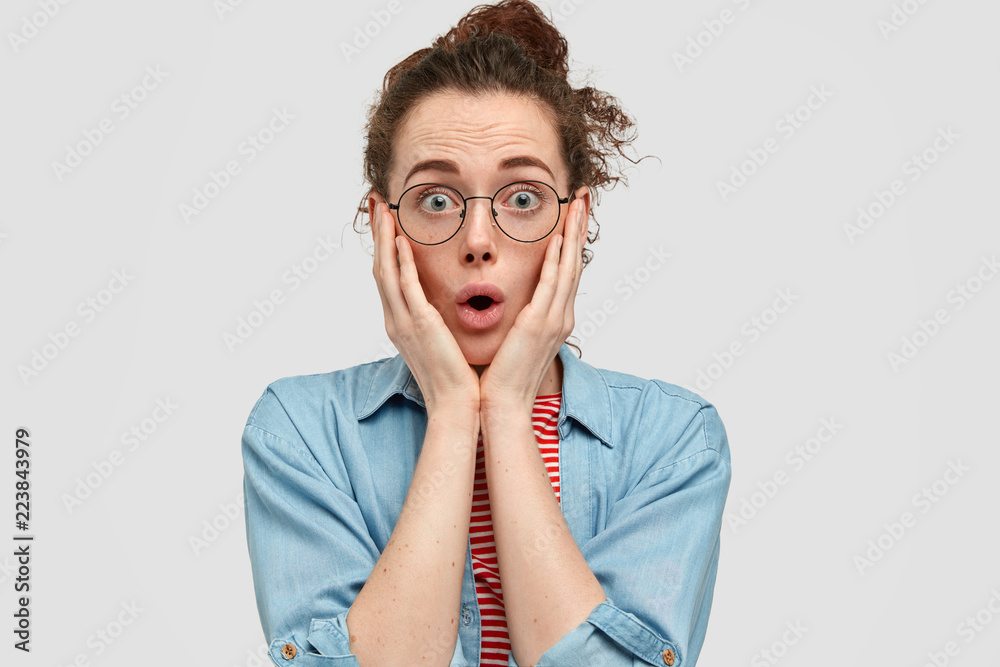 Stunned European girl has stupefied expression, opens mouth, keeps both ...