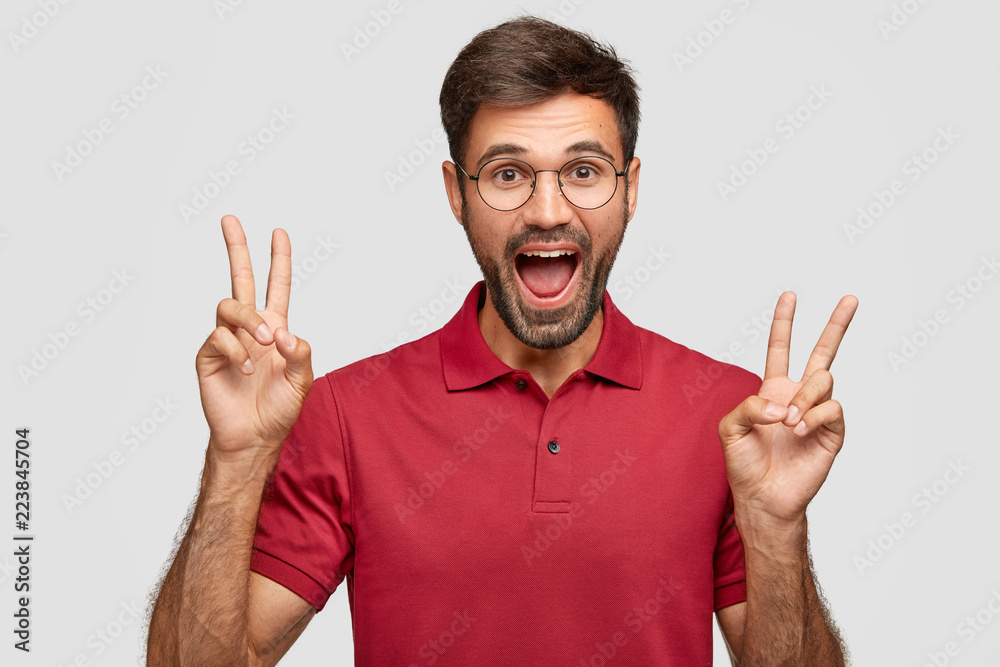 Optimistic glad unshaven man with positive facial expression, shows V ...