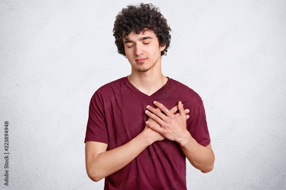 Thankful young boy keeps hands on heart, being touched by heart ...