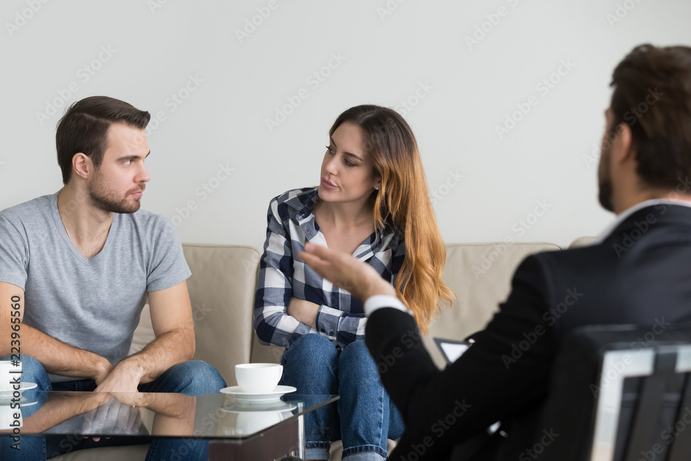 Angry divorcing couple sit on couch looking at each other with hate and ...