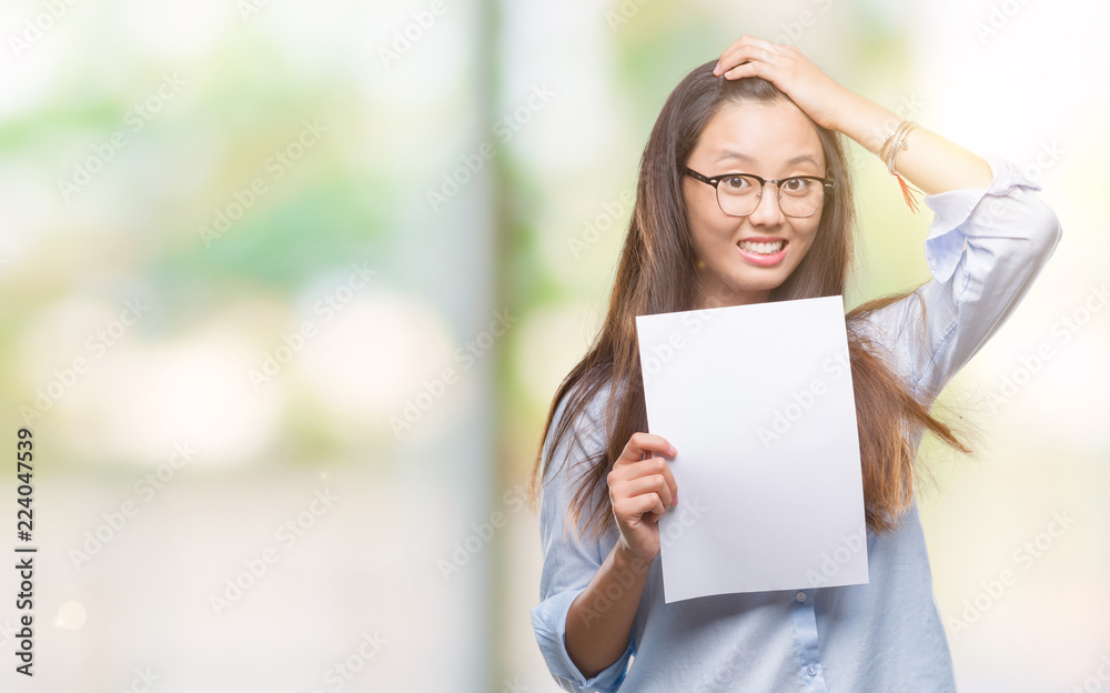 Young asian woman holding blank paper over isolated background stressed ...