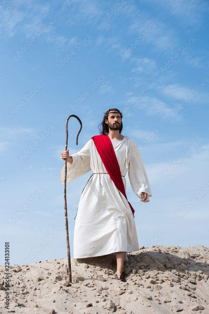 Jesus in robe, red sash and crown of thorns standing on sandy hill with ...