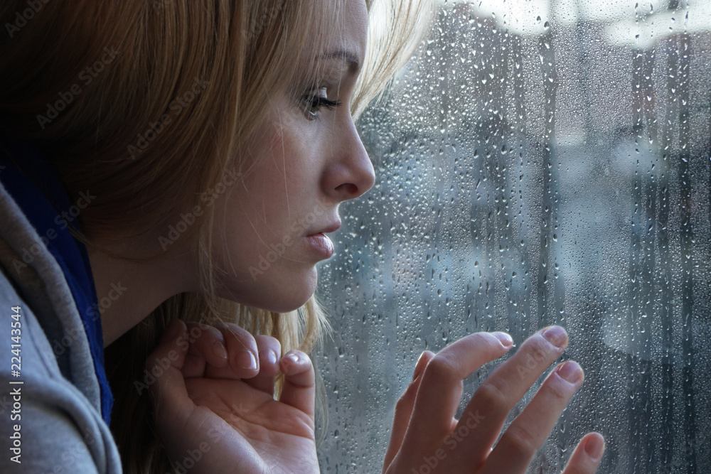 sad young woman looking through window on rainy day. depression concept ...