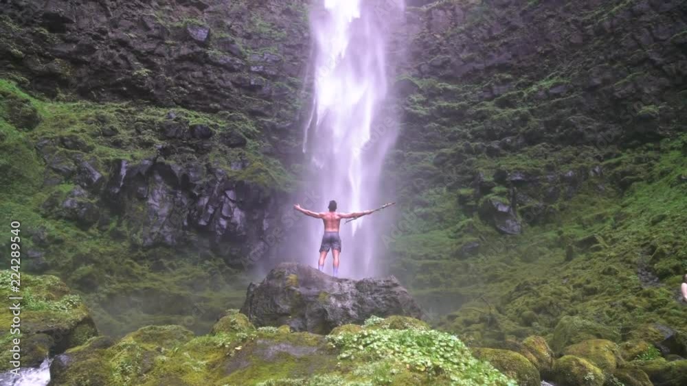 Video Stock Man stands tall raising arms with a tall waterfall in front ...
