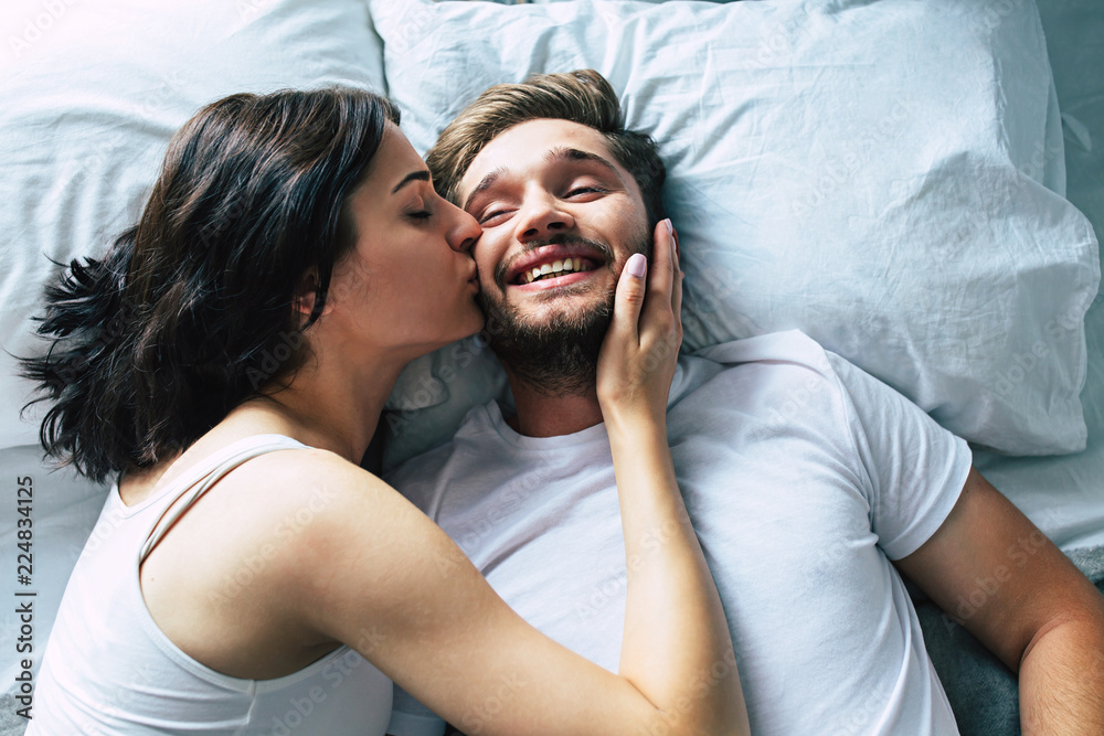 Happy beautiful young couple are lying, hugging and kissing in a ...