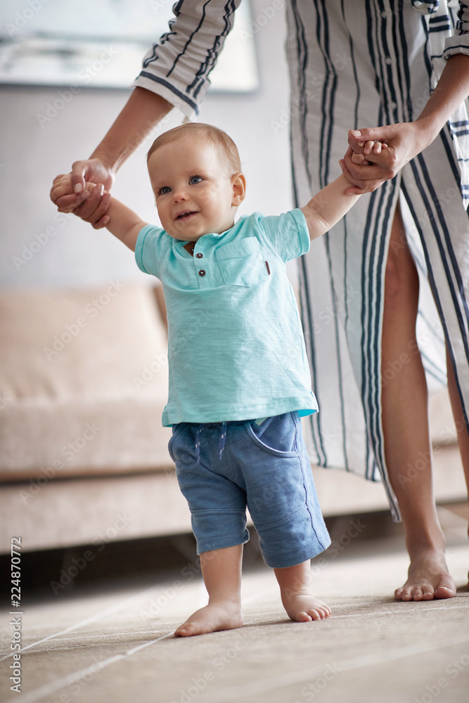 Smiling baby learning walking with mother, child enjoys the first steps ...